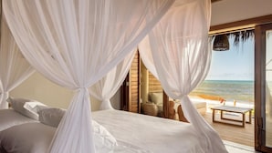 Quarto com cama grande, cortinas brancas e vista para o oceano.