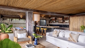 Uma sala de estar espaçosa com teto de madeira, um sofá branco, uma mesa de centro e uma TV ao fundo.