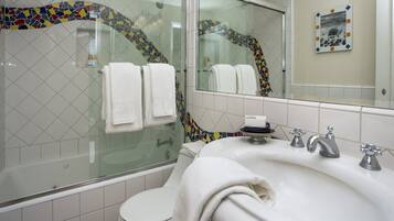 Casa de banho com chuveiro em cabine de vidro, lavatório branco com duas torneiras e sanita.