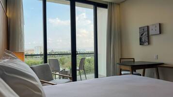 Quarto de hotel com uma janela grande, uma cama, uma escrivaninha e duas cadeiras.