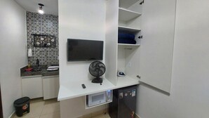Uma cozinha compacta com televisão integrada, micro-ondas e frigorífico pequeno.