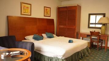 Quarto de hotel com cama, escrivaninha, cadeira, luminária e duas imagens emolduradas na parede.