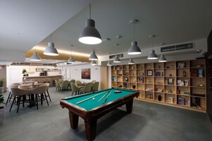 Uma mesa de bilhar em um espaço com área de refeições, estantes de livros e iluminação pendente.