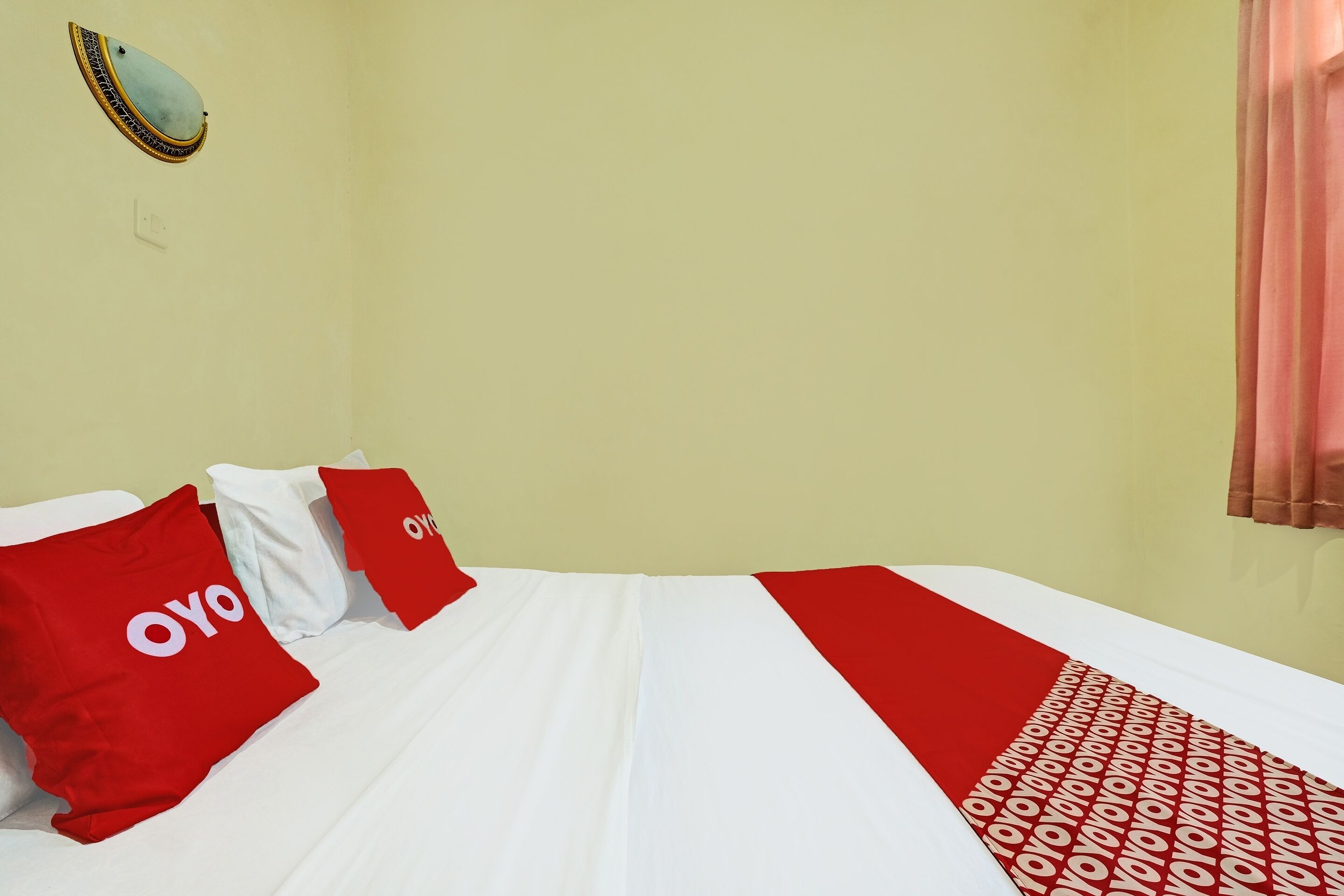 Quarto de hotel com cama, roupa de cama branca, almofadas vermelhas e manta estampada.