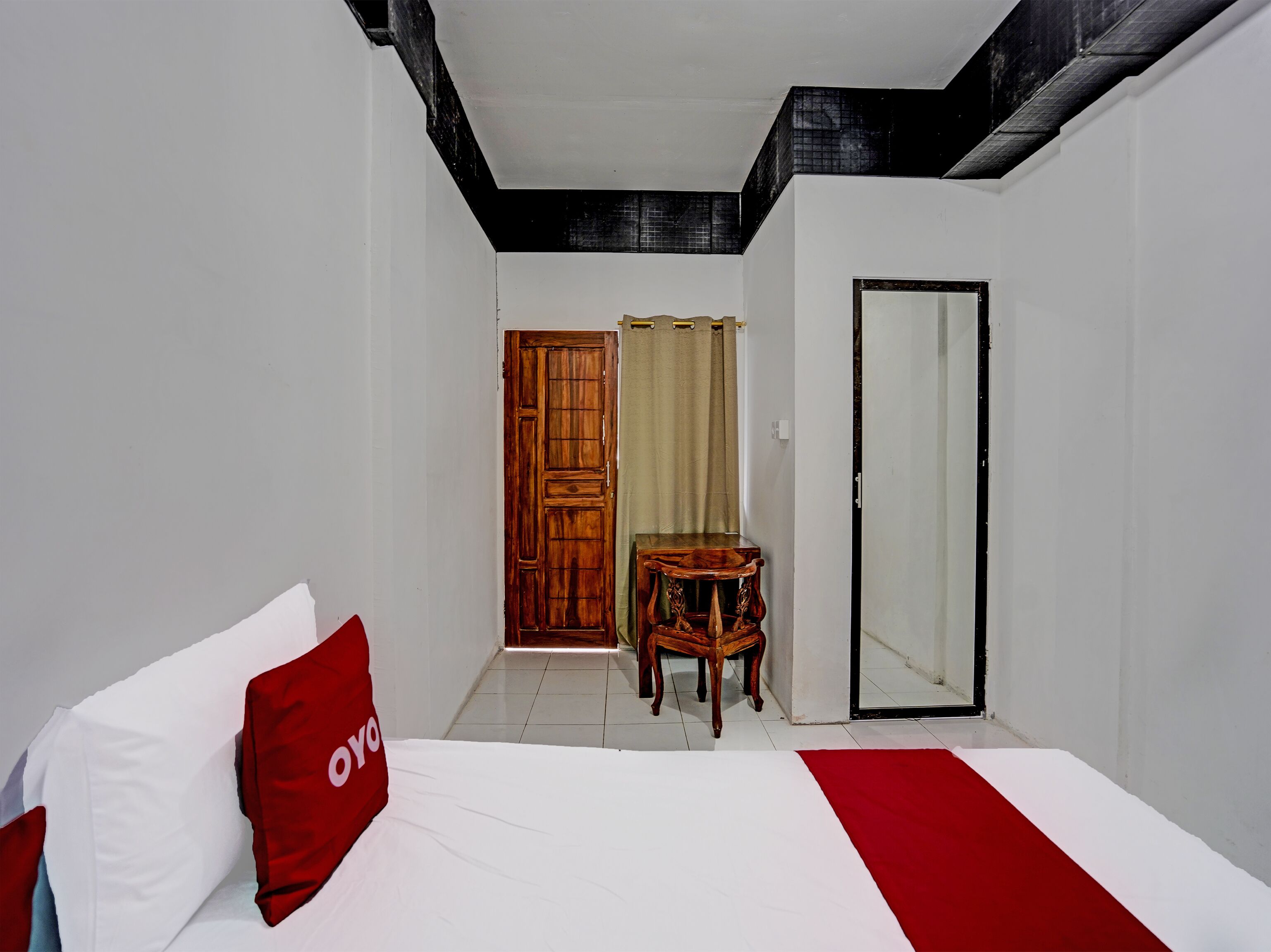 Quarto de hotel com uma cama, uma cadeira de madeira, um espelho e uma porta.