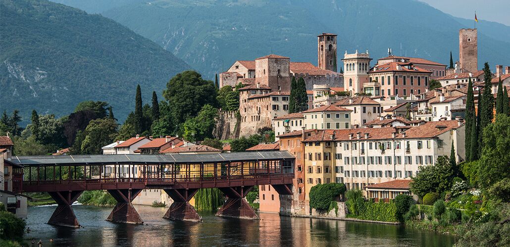 Uma cidade histórica com uma ponte notável sobre um rio, rodeada por vegetação exuberante e montanhas.
