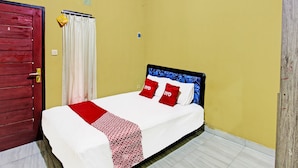 Quarto de hotel com uma cama, uma porta vermelha, uma janela com cortinas e um ar condicionado fixado na parede.