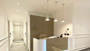 Balcão de recepção moderno com divisória de vidro, iluminação pendente no teto e telefone fixado na parede.
