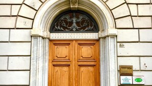 Uma porta dupla de madeira com um arco decorativo acima, embutida em um edifício com fachada de pedra.