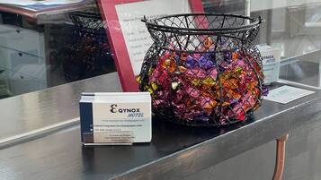 Uma área de recepção de hotel com uma vitrine de vidro contendo itens coloridos embalados e um aviso com informações de contato do hotel.