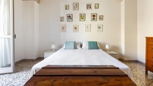 Quarto com cama, duas mesas de cabeceira, cômoda de madeira e parede decorada com gravuras botânicas.