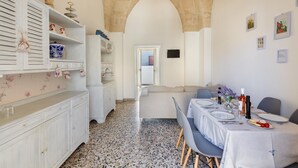 Uma área de refeições com uma mesa posta para dois, um armário branco com objetos decorativos e um teto de pedra.