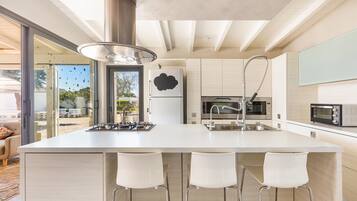 Uma cozinha moderna com ilha central, eletrodomésticos de aço inoxidável e uma grande janela com vista para um pátio.