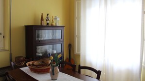 Uma área de refeições com mesa de madeira, cadeiras, um armário com portas de vidro e um vaso com flores.
