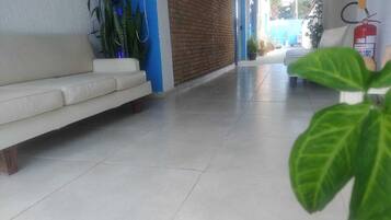 Um corredor com um sofá bege, plantas em vasos e um extintor de incêndio.