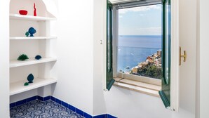 Quarto com janela que dá para a costa, paredes brancas e azulejos no chão com padrão azul.