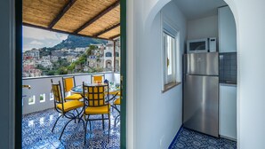 Varanda com cadeiras amarelas e uma mesa, cozinha equipada com frigorífico e micro-ondas, e vista para a paisagem urbana.