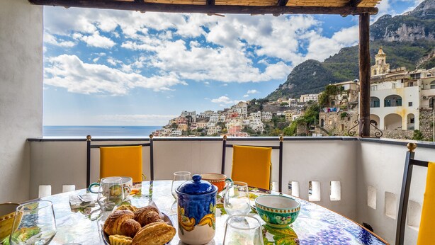 Mesa posta para o café da manhã, com vista para uma cidade costeira e montanhas.