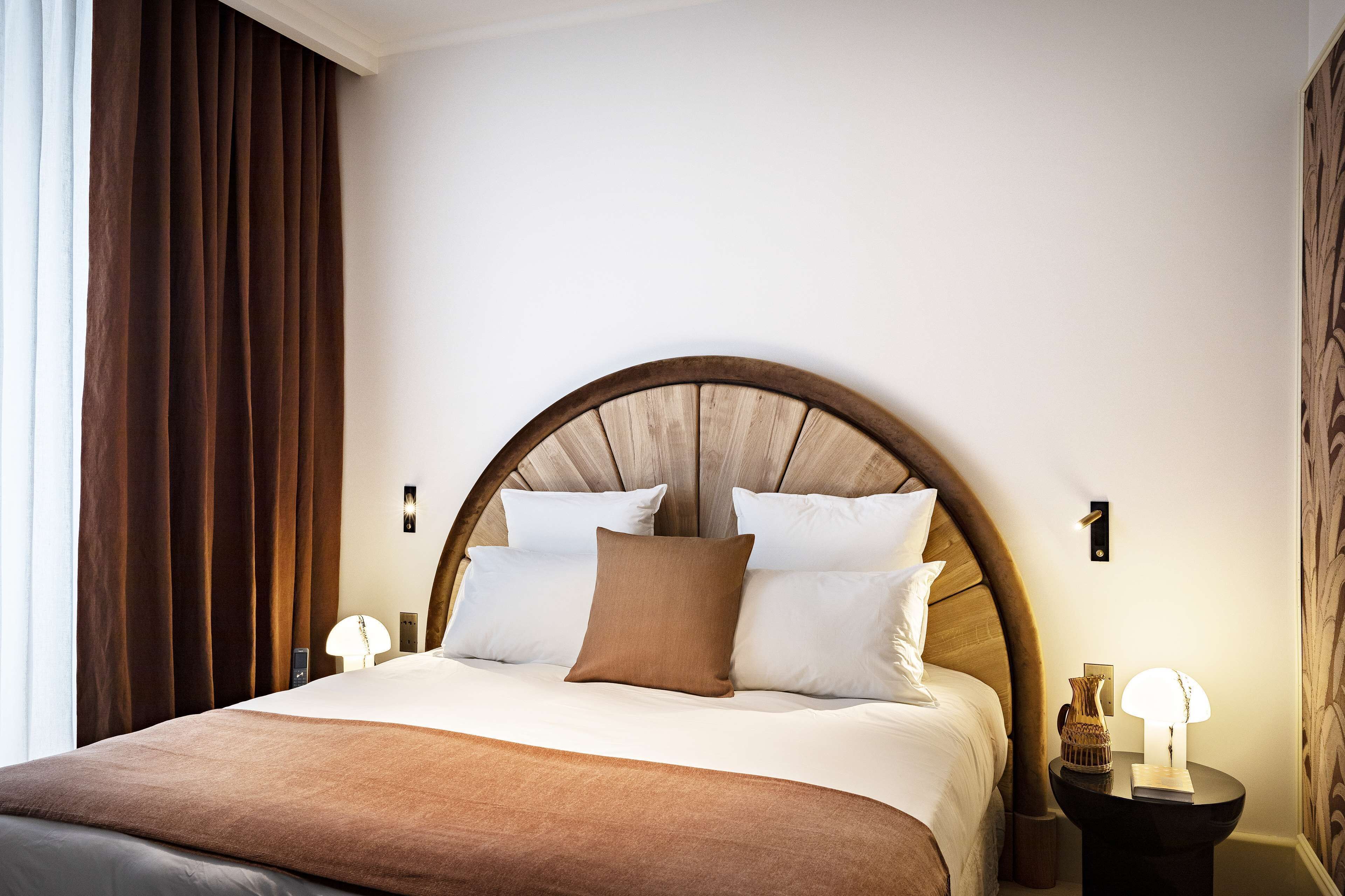 Cama bem arrumada com cabeceira de madeira, manta marrom e duas luminárias em um criado-mudo.
