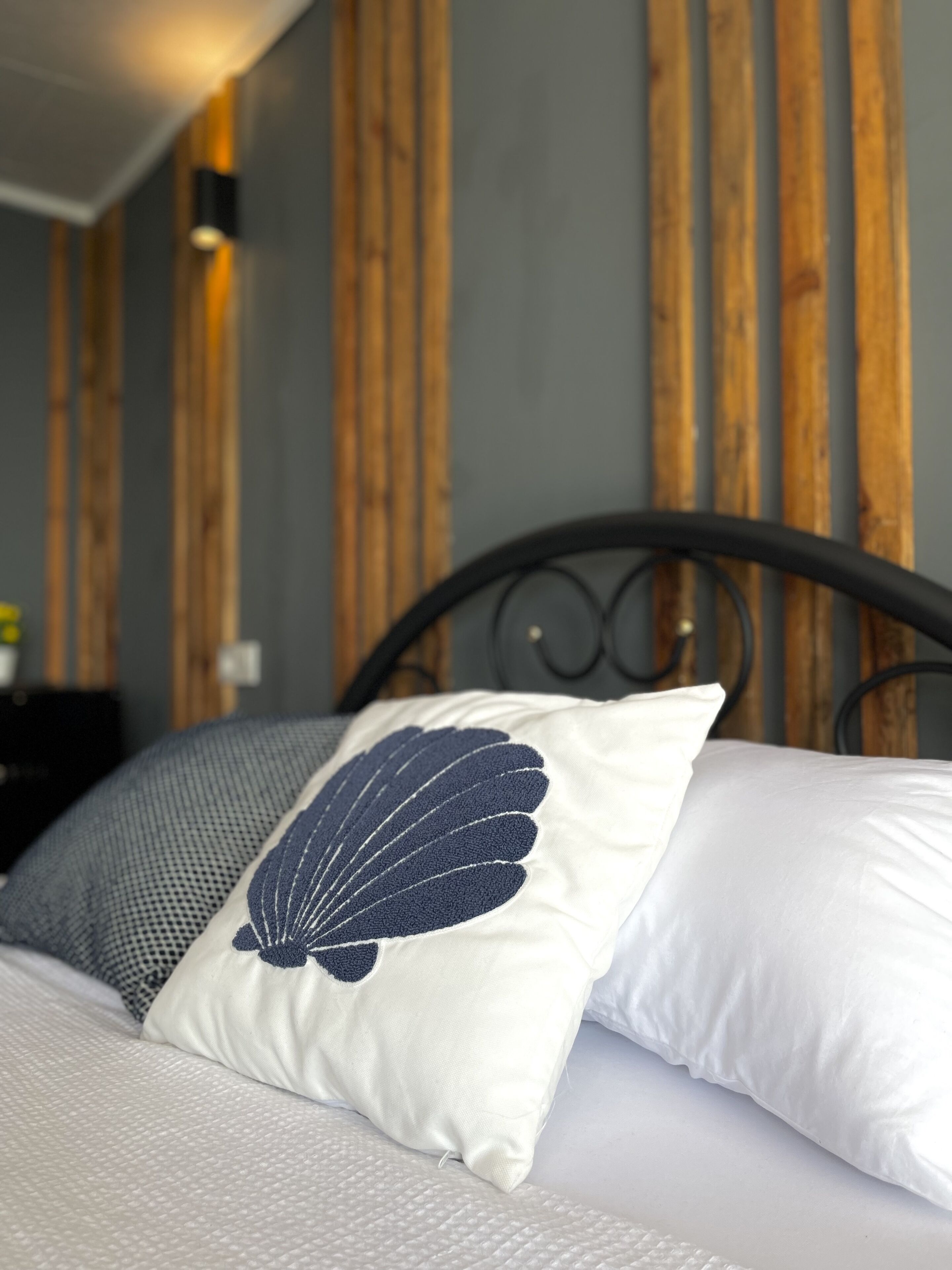 Uma cama com travesseiro azul-marinho e branco, um travesseiro cinza estampado e um edredom branco texturizado.