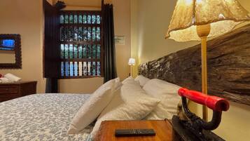 Quarto de hotel com cama, cabeceira de madeira, mesa de cabeceira com luminária e televisão em uma cômoda.