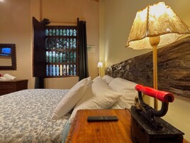 Quarto de hotel com cama, cabeceira de madeira, mesa de cabeceira com luminária e televisão em uma cômoda.