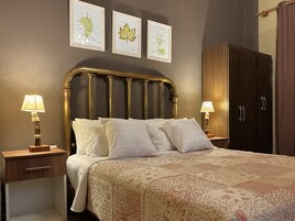 Cama bem arrumada com colcha estampada, duas luminárias de cabeceira e gravuras botânicas emolduradas na parede.