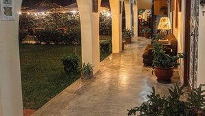 Um corredor com arcos que levam a um jardim, plantas em vasos e um candeeiro.
