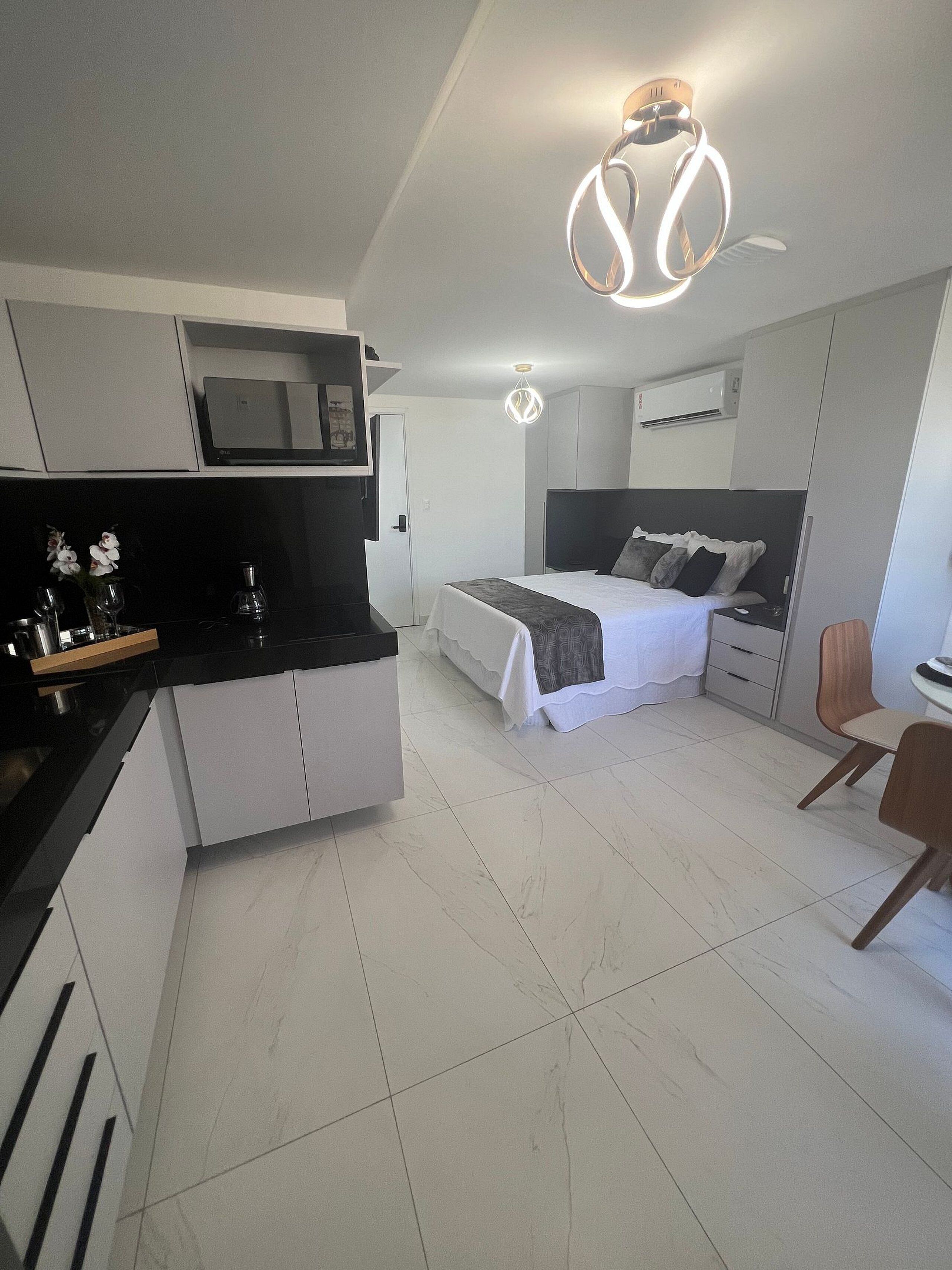 Quarto de hotel compacto com cozinha compacta, uma cama com cabeceira, mesa de cabeceira e uma cadeira.