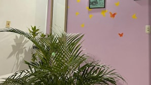 Quarto com teto de madeira, parede roxa com adesivos de borboletas, um certificado emoldurado e um vaso com planta.