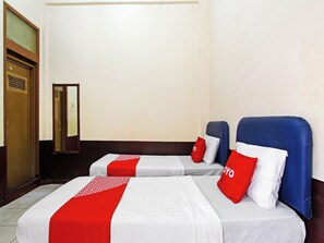 Quarto de hotel com duas camas, cada uma com colcha vermelha e branca e almofadas combinando.