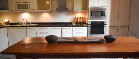 Uma cozinha moderna com armários brancos, eletrodomésticos de aço inoxidável e uma mesa de jantar de madeira.