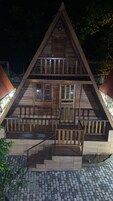 Uma cabana de madeira com dois andares, com uma varanda no andar superior e uma escada que leva à entrada.