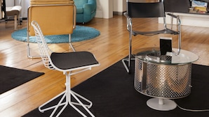 Uma sala de estar moderna com uma poltrona verde-água, uma cadeira preta e branca, uma mesa de centro redonda e um lustre.