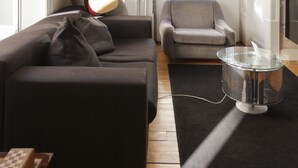 Uma sala de estar com sofá, um violão, uma cadeira e um radiador.