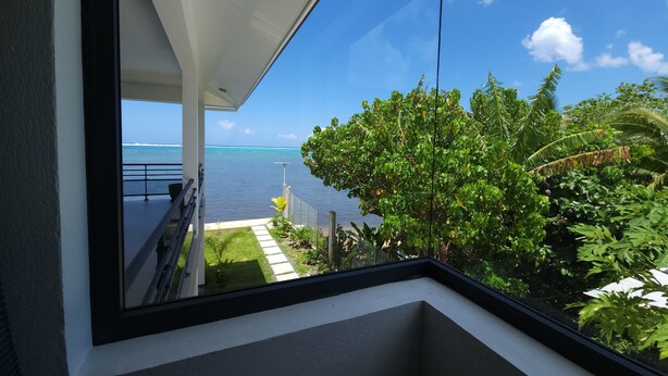 Vista de uma varanda com céu claro, oceano e vegetação exuberante.