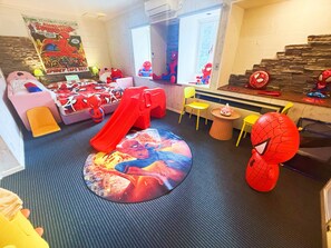 Um espaço de brincadeiras infantil com escorrega, decoração do Homem-Aranha e um pôster grande na parede.