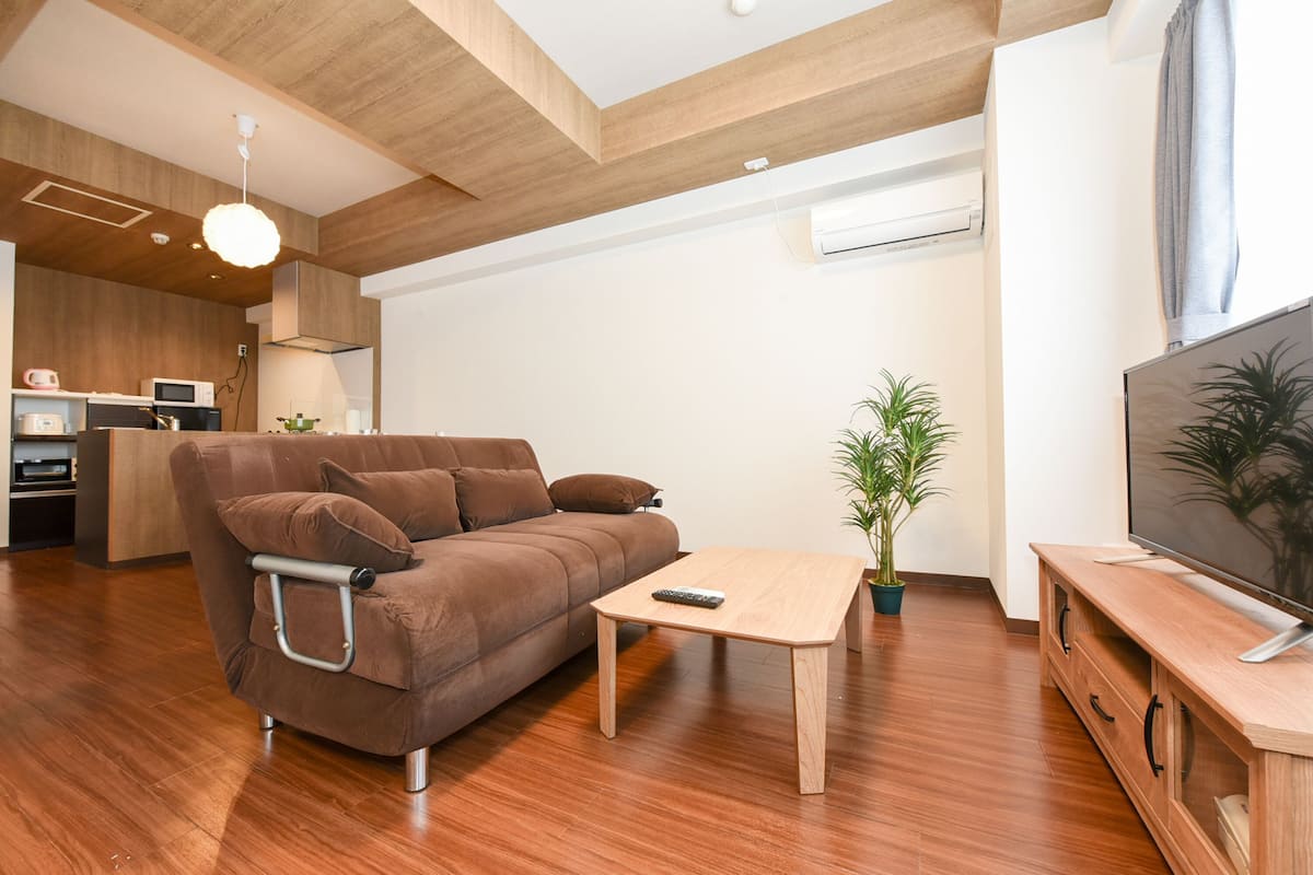 Uma sala de estar moderna com um sofá marrom, uma mesa de centro de madeira e uma televisão sobre um suporte de madeira.
