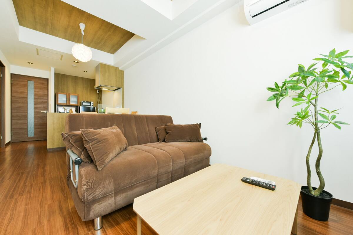 Uma sala de estar moderna com um sofá marrom, uma mesa de centro de madeira e uma planta em vaso.