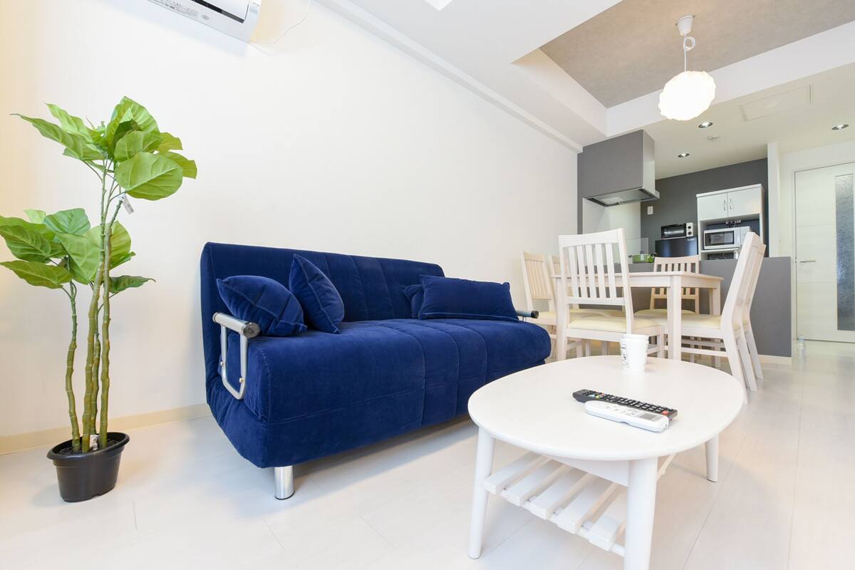Uma sala de estar moderna com um sofá azul, uma mesa branca e um vaso de planta.