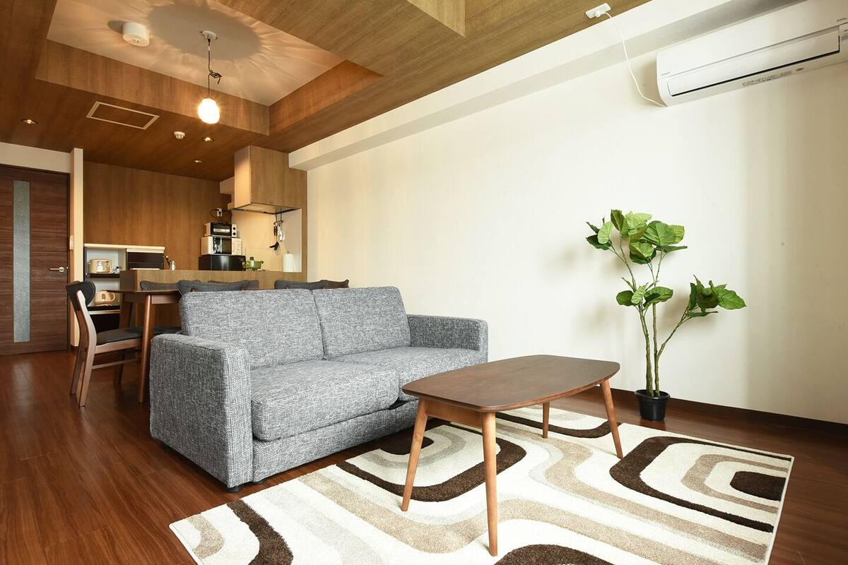 Um espaço de estar compacto com um sofá cinzento, uma mesa de centro de madeira e um vaso com planta.