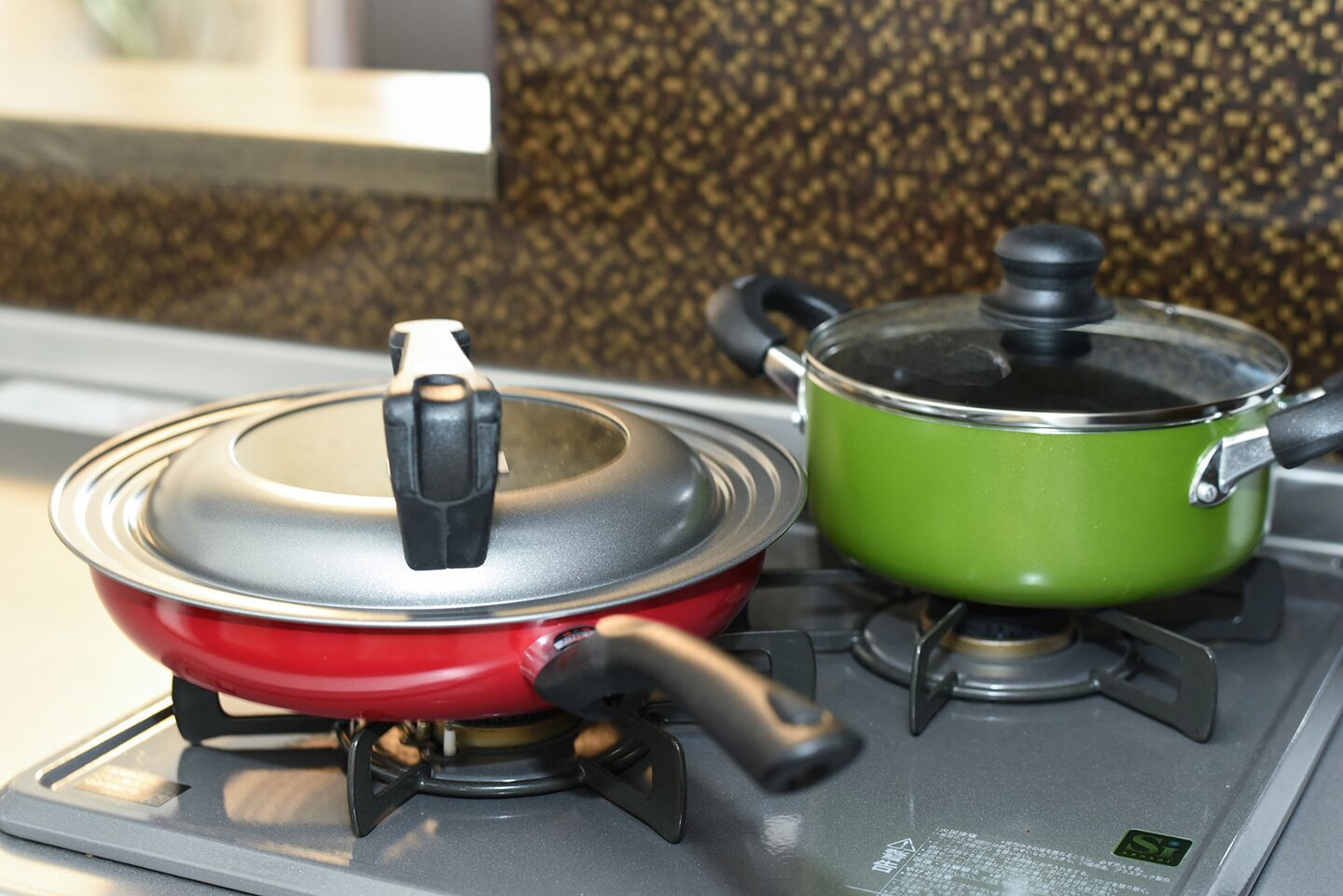 Um fogão com duas panelas, uma vermelha e outra verde, em uma bancada de cozinha.
