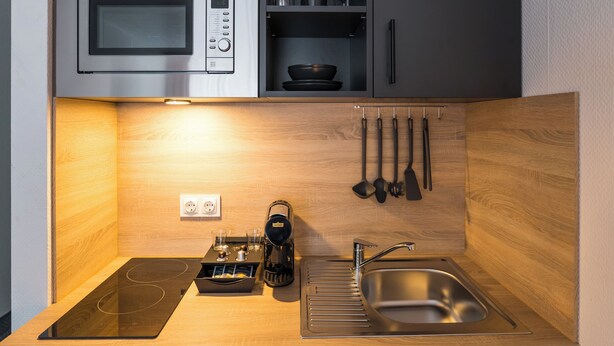 Uma cozinha compacta com micro-ondas embutido, cafeteira e pia.