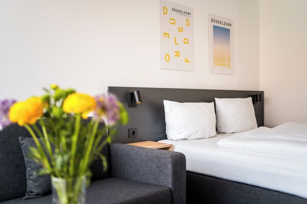Quarto de hotel com cama, mesa de cabeceira, abajur e um vaso com flores.