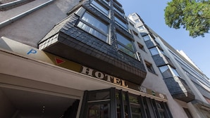 Entrada de hotel com um letreiro chamativo 'HOTEL', sinal de estacionamento e escadaria que leva à entrada.