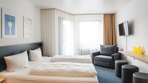 Quarto de hotel com cama, secretária, cadeira e televisão.