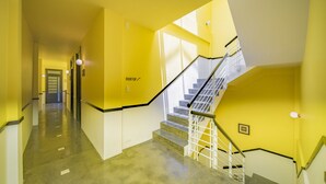 Um corredor com escada que leva a um andar superior, com uma parede amarela e uma placa que diz "ROOFTOP".