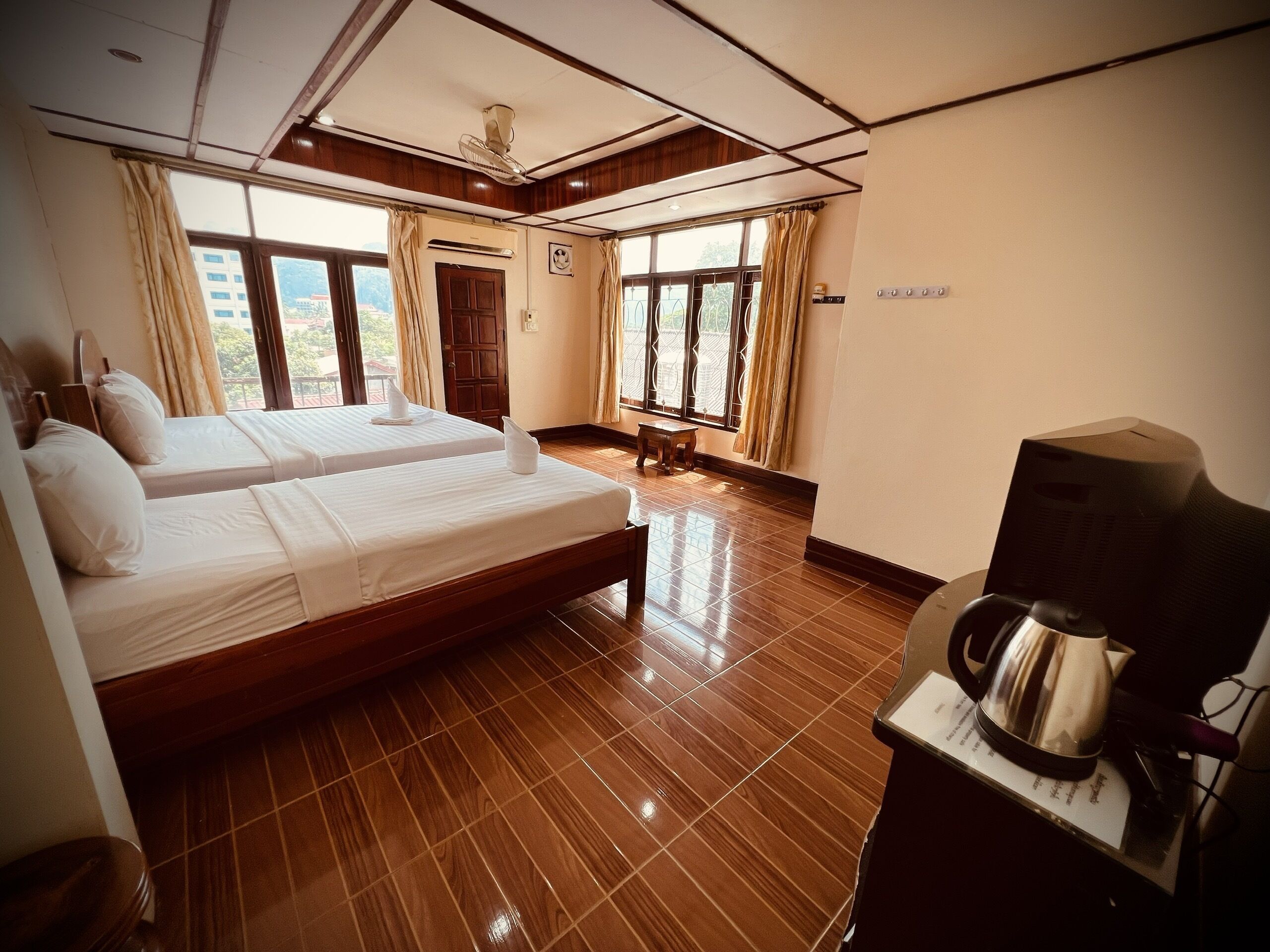 Quarto de hotel com duas camas, piso de madeira, televisão e janela com cortinas.