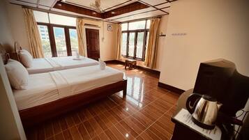 Quarto de hotel com duas camas, piso de madeira, televisão e janela com cortinas.