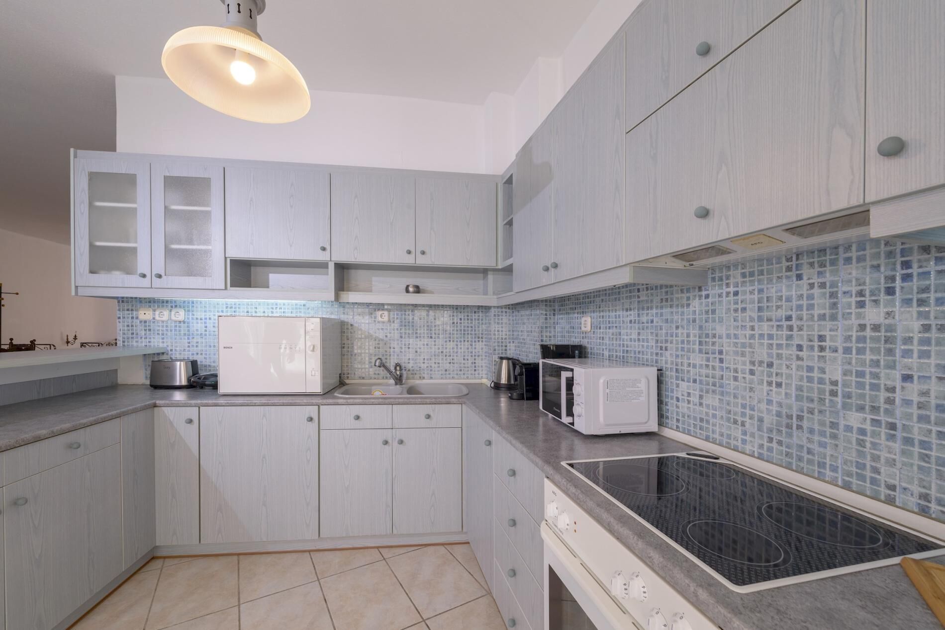 Uma cozinha com armários de madeira clara, painel de azulejos, micro-ondas embutido e fogão a gás.